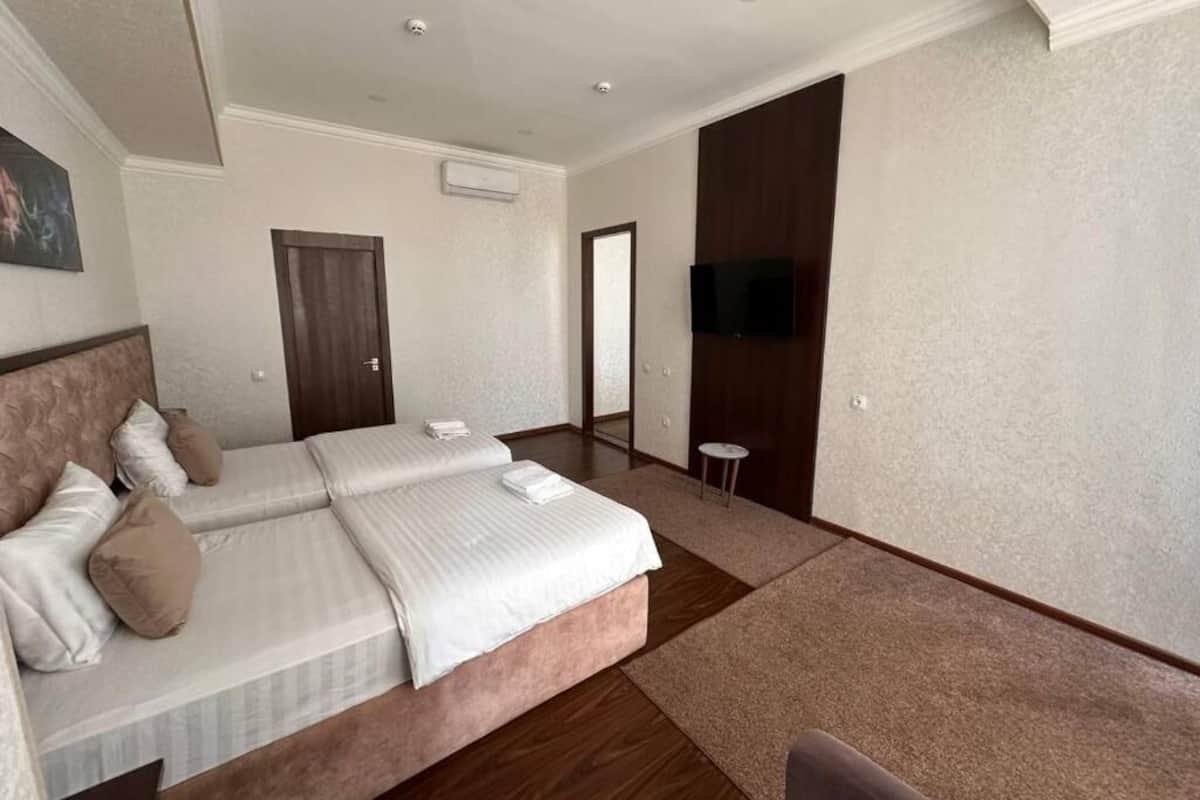 Quarto de hotel com uma cama grande, televisão, porta e uma pequena mesa.