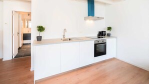 Cozinha moderna com armários brancos, forno embutido e bancada com pia e chaleira.
