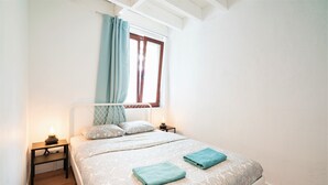 Quarto com cama, mesas de cabeceira, janela com cortinas e mesa de apoio com abajur.