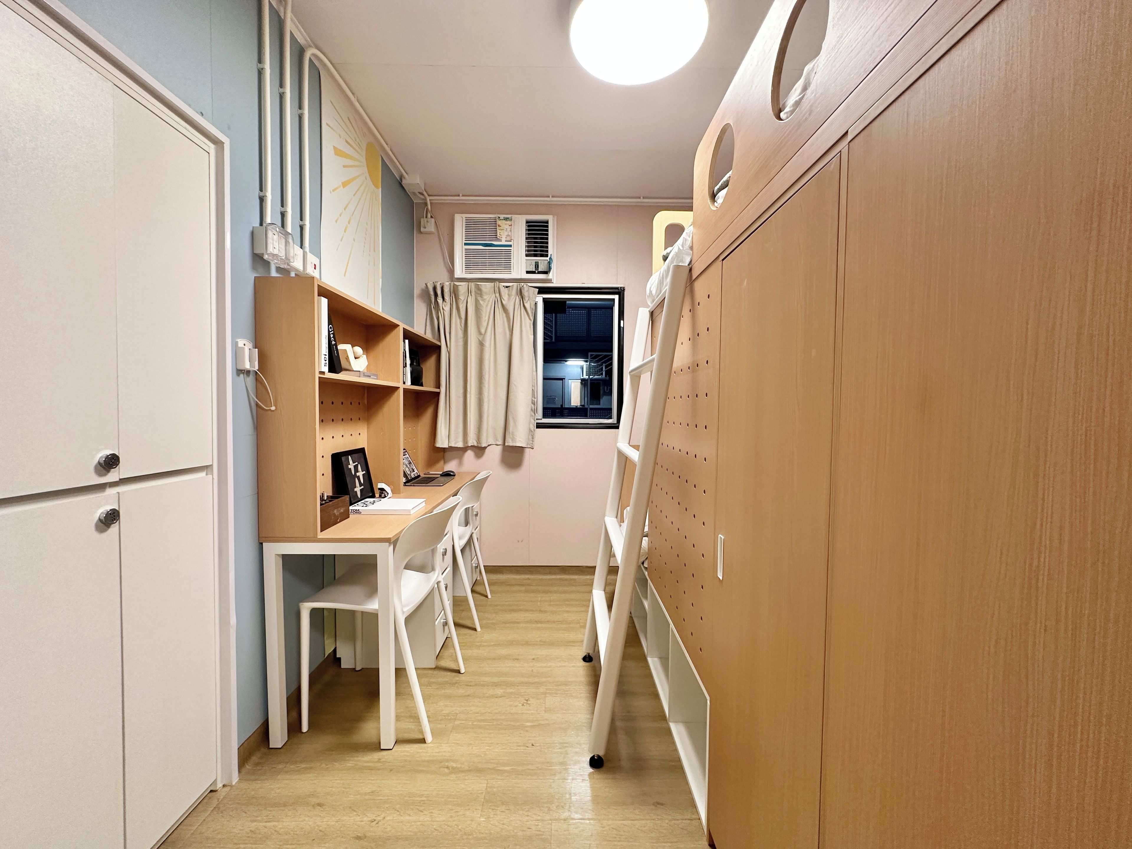 Um corredor estreito com uma mesa, cadeiras e um guarda-roupa.