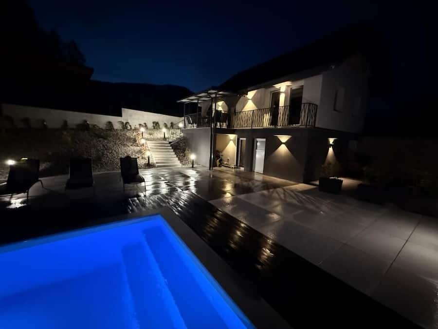 Uma casa moderna com piscina, varanda coberta e escada que leva a um segundo andar.