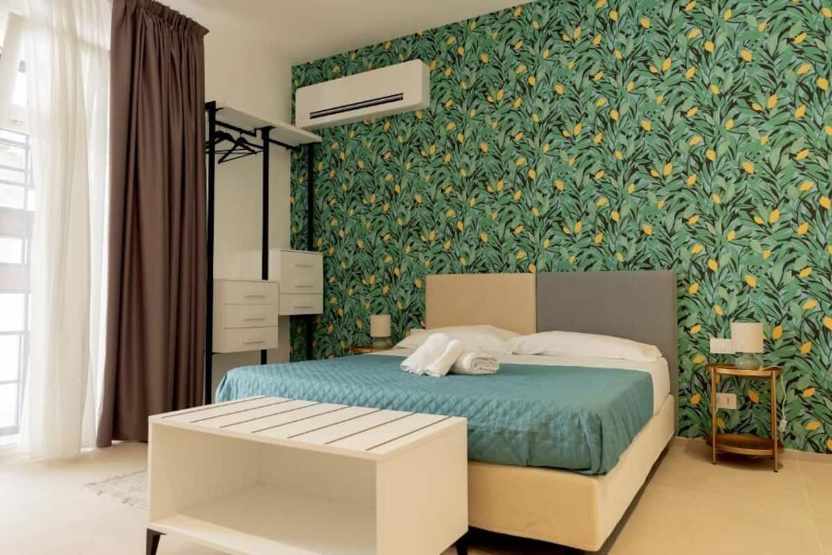 Quarto com cama, mesa de cabeceira, guarda-roupa e ar condicionado.