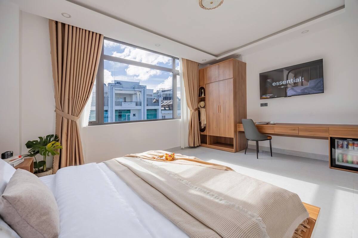 Quarto de hotel moderno com cama grande, escrivaninha, televisão e vista para a paisagem urbana.