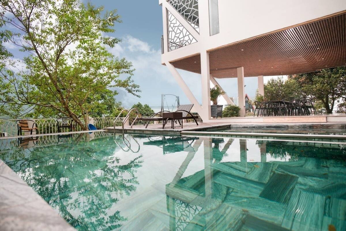 Piscina cristalina com espreguiçadeiras e um edifício moderno com fachada geométrica.