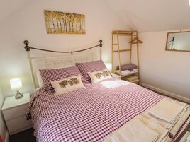 Uma cama bem arrumada com colcha xadrez, uma luminária de cabeceira, uma escada de madeira e um quadro na parede.