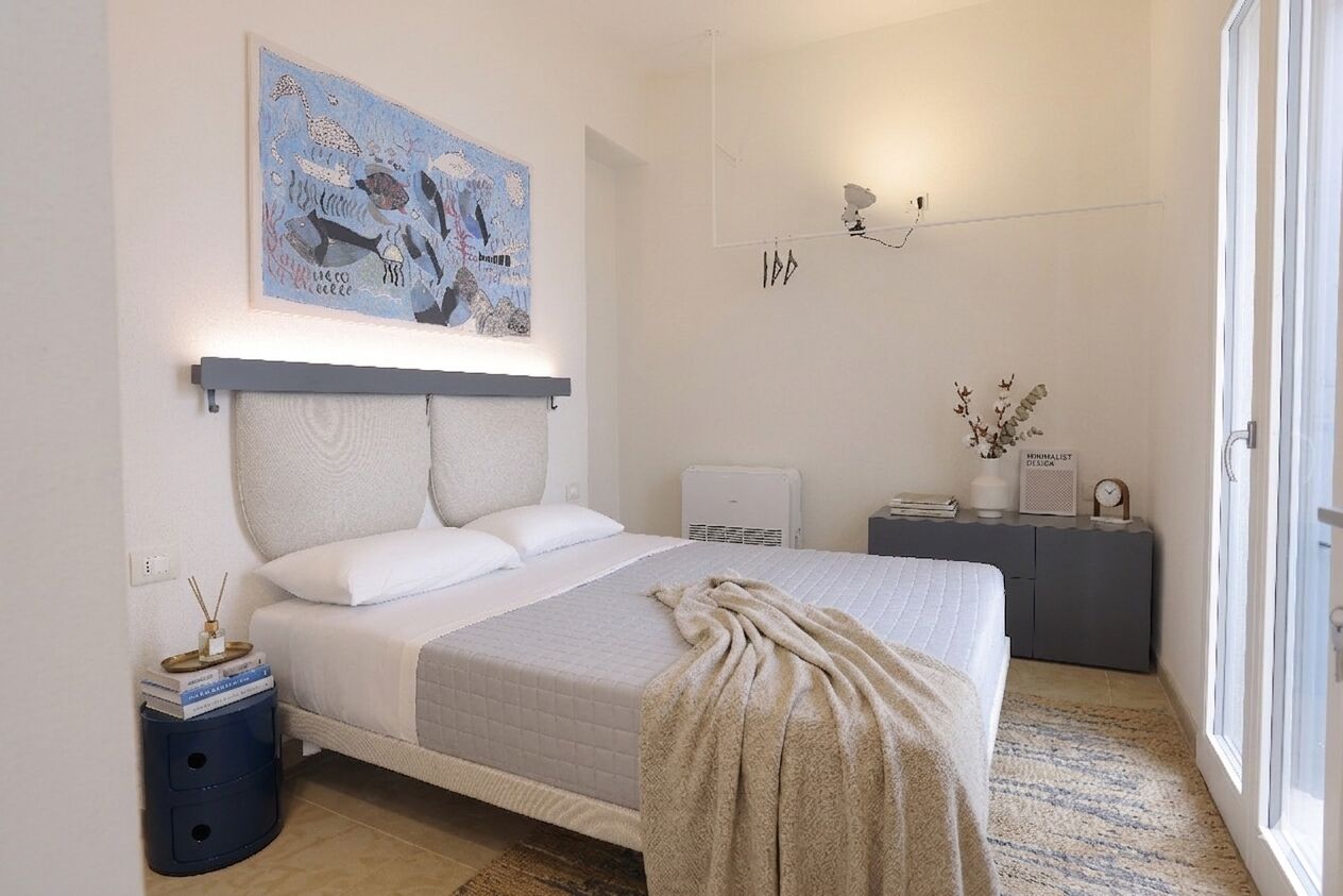 Quarto com cama, mesa de cabeceira, obras de arte na parede e uma janela.