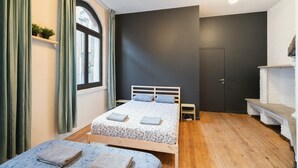 Quarto com cama, mesa de cabeceira, guarda-roupa, janela com cortinas e estante com plantas.