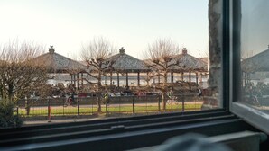 Visão pela janela de um edifício com arquitetura tradicional, incluindo uma série de estruturas cobertas e uma área cercada com pessoas e bicicletas.