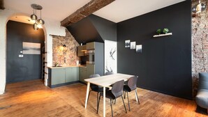 Cozinha moderna com parede de tijolos, piso de madeira e área de jantar com mesa e cadeiras.