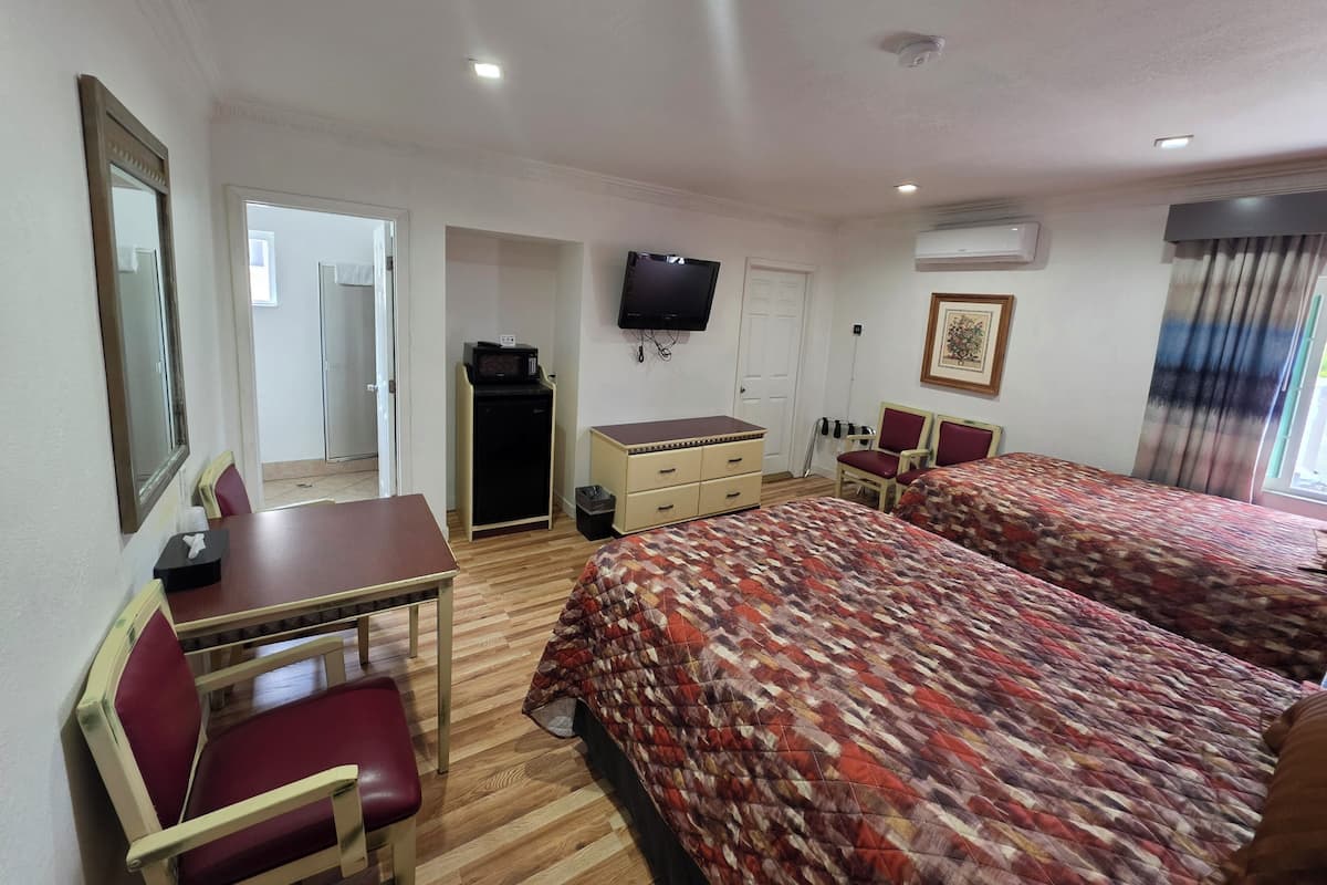 Quarto de hotel com duas camas, uma mesa com cadeira, televisão, cómoda e porta para outro quarto.