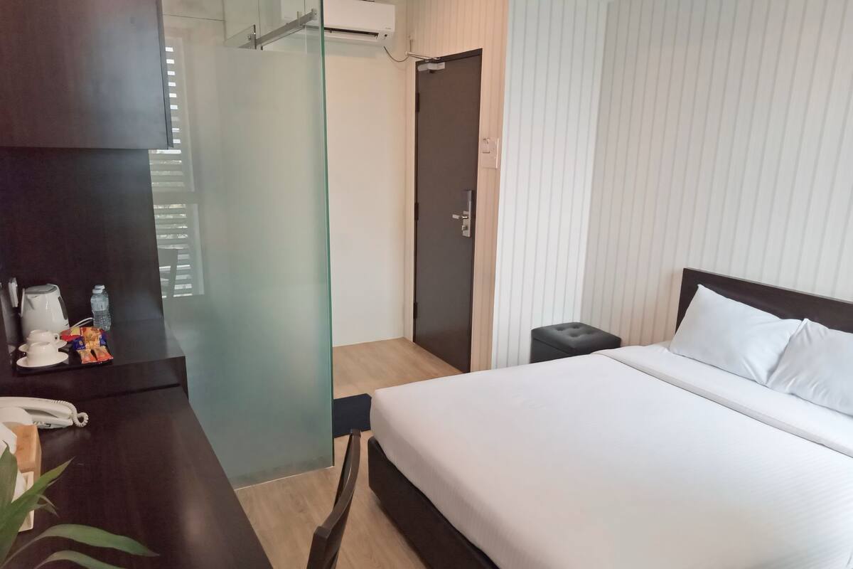 Quarto de hotel com cama, mesa de cabeceira, escrivaninha com telefone, cafeteira e garrafa de água.