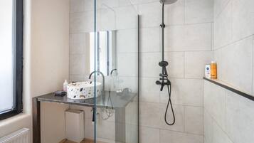 Uma casa de banho moderna com cabine de duche em vidro, uma sanita branca com espelho e uma pequena prateleira com artigos de higiene pessoal.