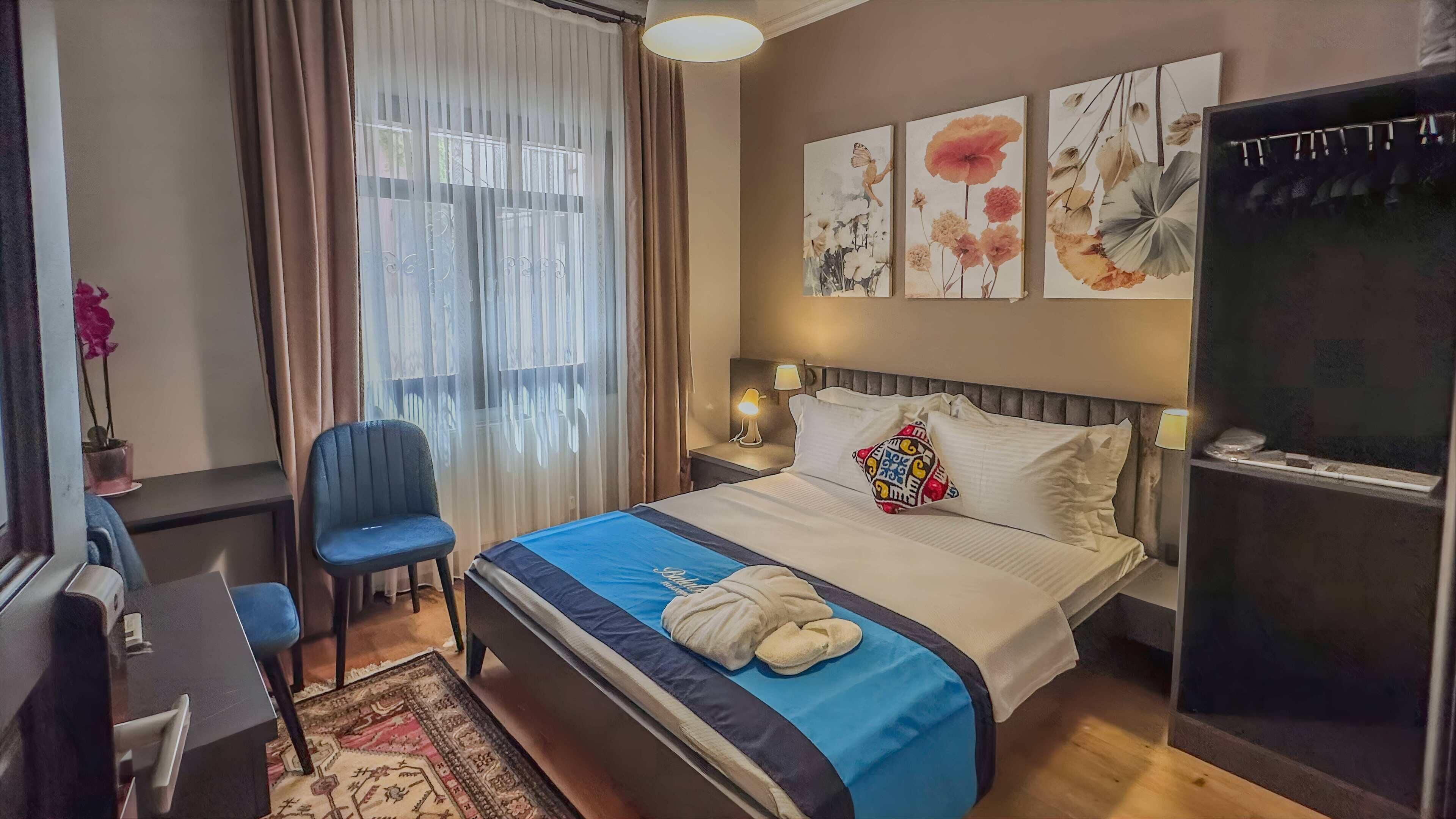 Quarto de hotel com cama, escrivaninha, cadeira, televisão e obras de arte na parede.