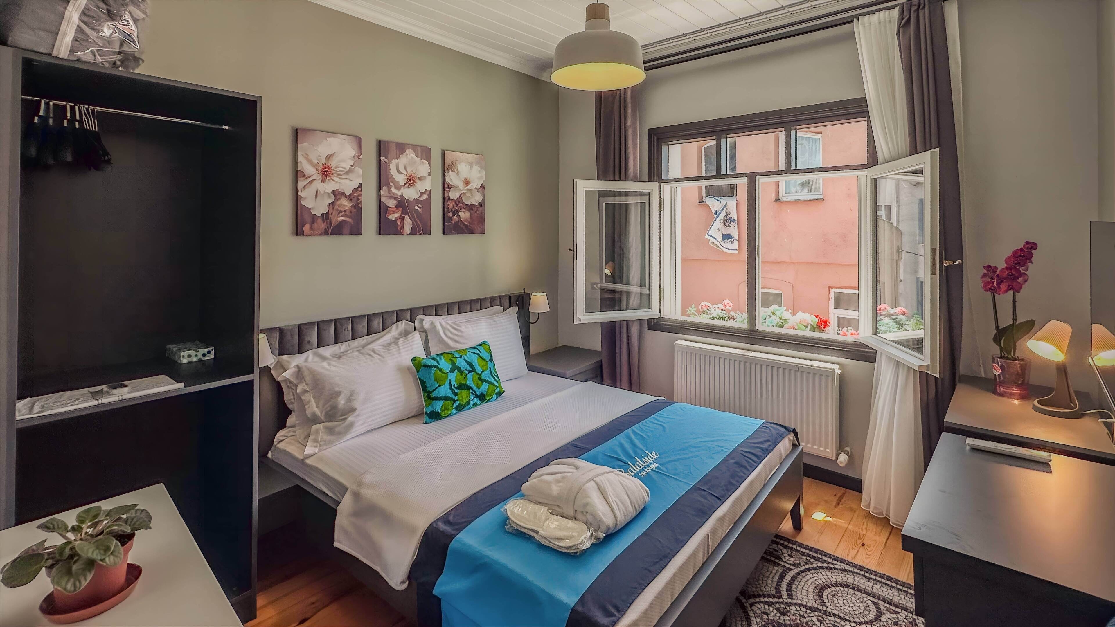 Quarto de hotel com cama, escrivaninha, janela com cortinas e vista para o exterior.