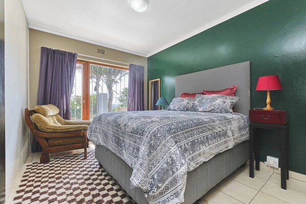 Um quarto com cama, uma cadeira, um abajur e vista para o exterior.