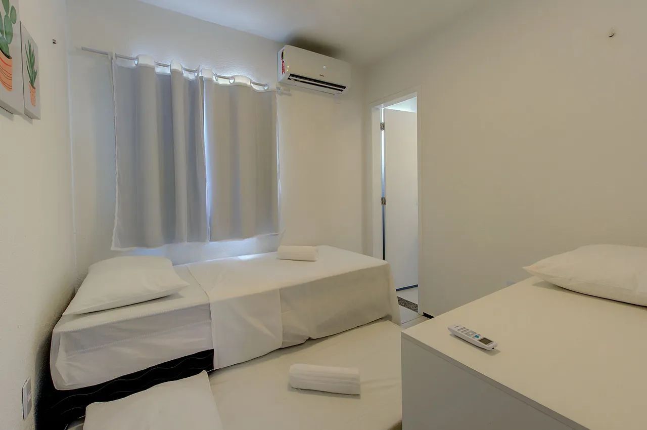 Quarto de hotel com duas camas, janela com cortinas, ar condicionado e um controle remoto na cama.