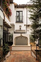 Um pátio com um muro de azulejos, uma varanda florida e uma escadaria que leva a uma porta.