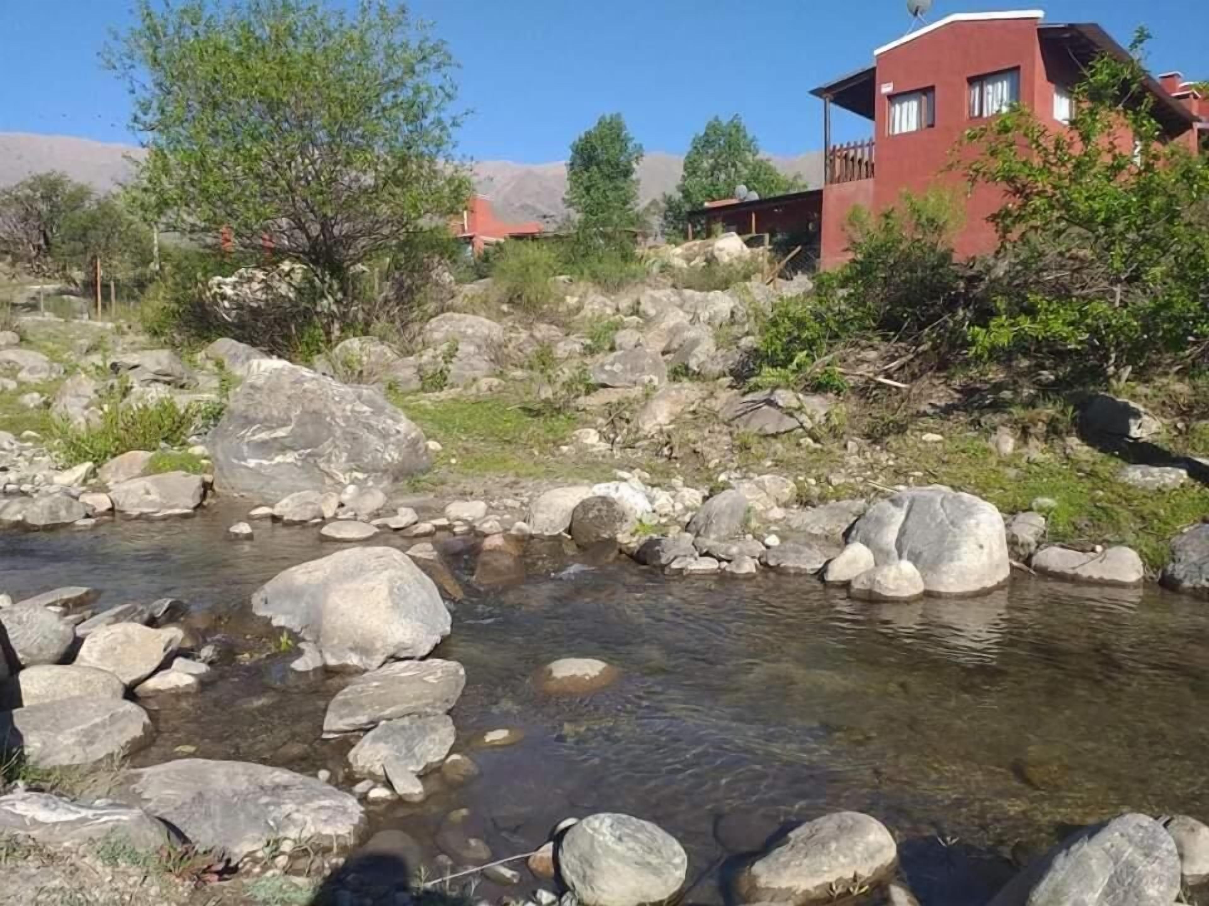 Ambiente natural ao ar livre com um riacho cristalino, pedras e vegetação.