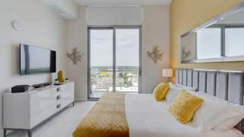 Quarto de hotel com cama, televisão, cômoda e uma grande janela com vista para a cidade.