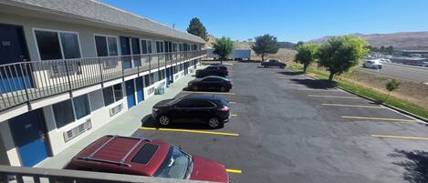 Um motel com uma fileira de vagas de estacionamento, um edifício com telhado plano e céu claro.
