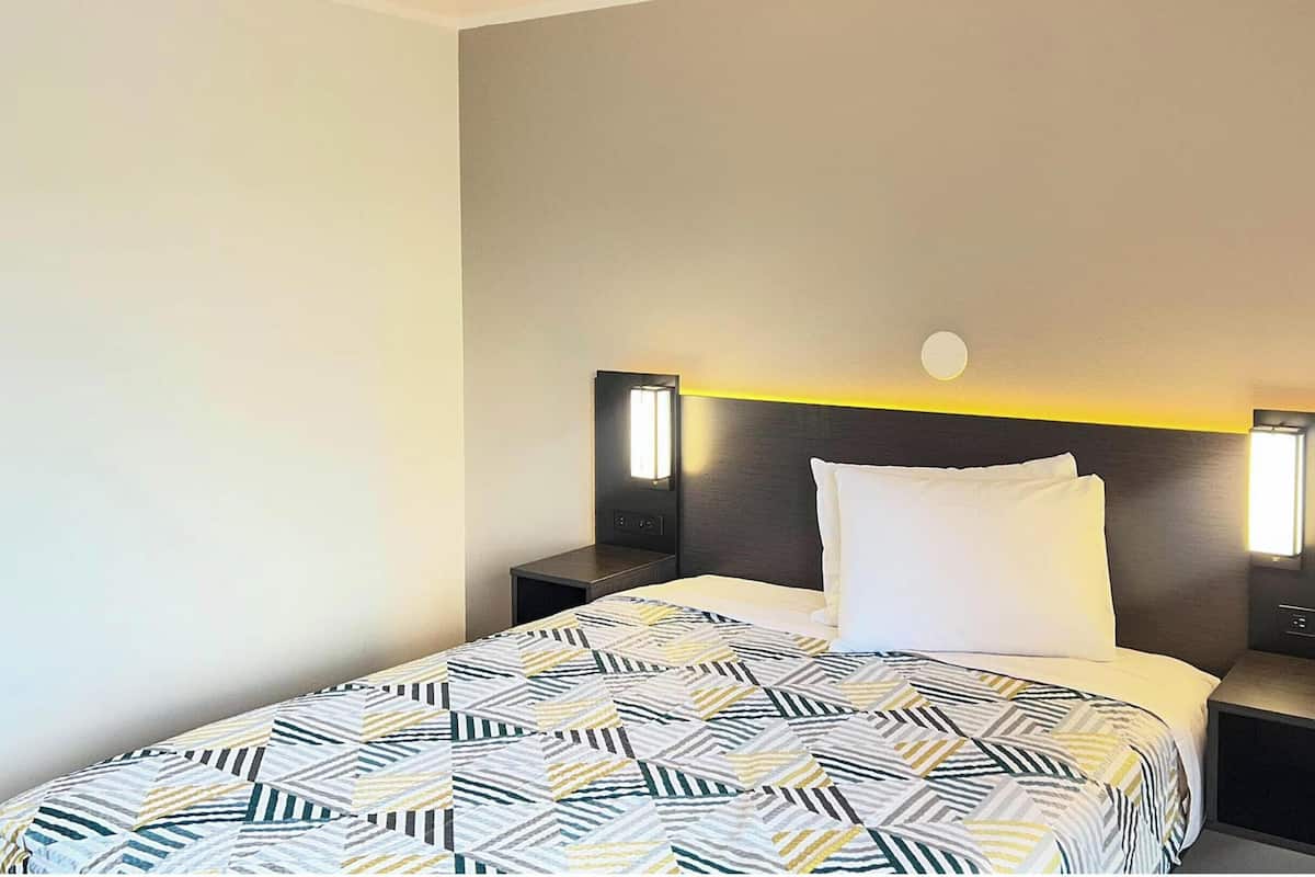 Quarto de hotel com uma cama, duas mesas de cabeceira e duas luminárias fixadas na parede.