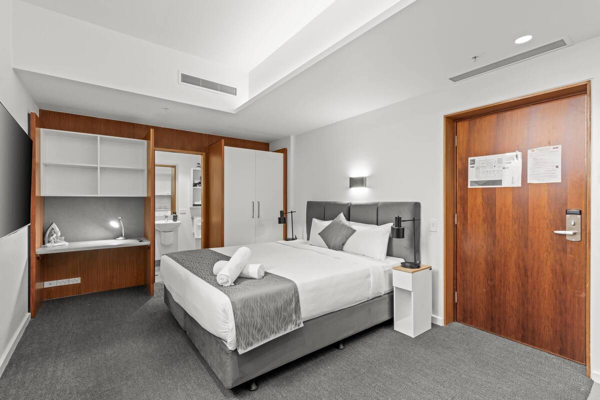 Quarto de hotel moderno com uma cama grande, uma escrivaninha, uma toucador e um guarda-roupa.