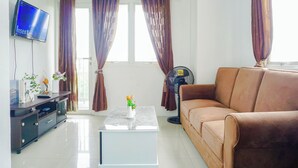 Uma sala de estar com sofá, televisão, mesa de centro, móvel para televisão e janela com cortinas.