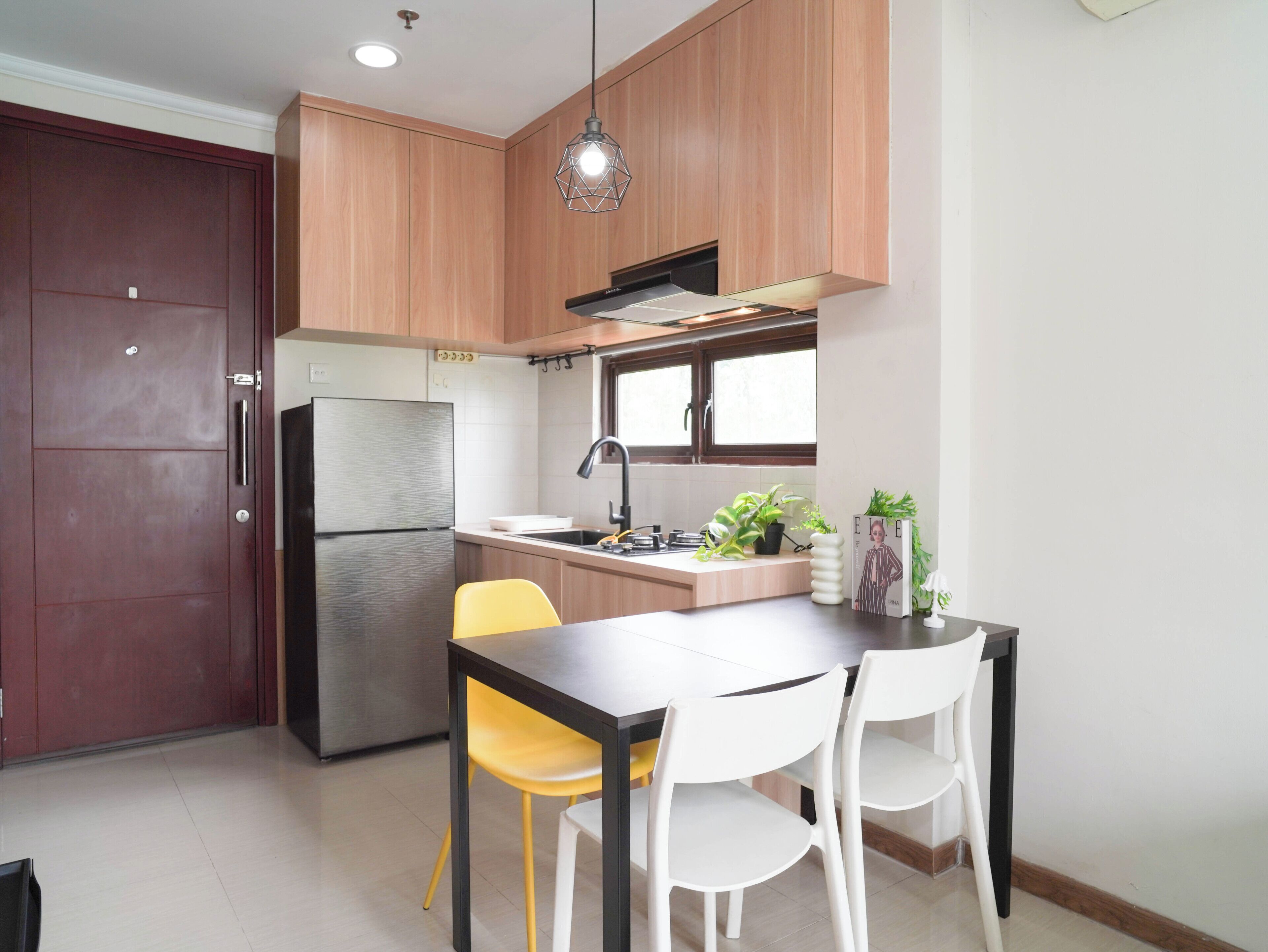 Cozinha compacta com armários de madeira, geladeira de aço inoxidável, pia e área de refeições com duas cadeiras.