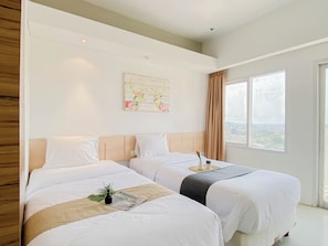 Quarto de hotel com duas camas, uma janela com vista para a cidade, um quadro na parede e uma pequena planta na mesa de cabeceira.