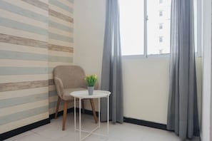 Quarto com parede listrada, uma cadeira, uma mesa pequena com uma planta e uma janela com cortinas.