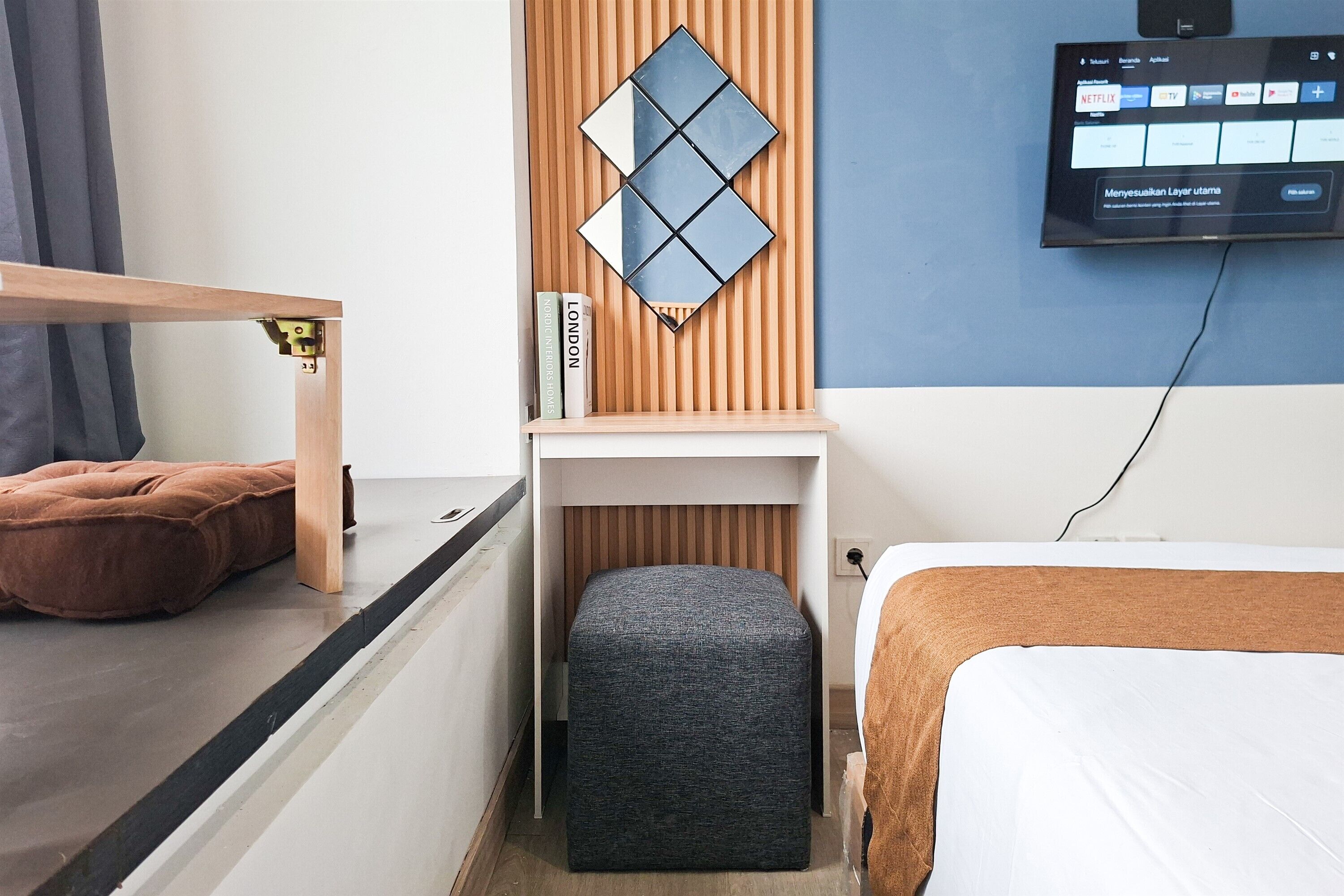 Quarto de hotel compacto com cama, pequena mesa de trabalho, televisão e espelho fixado na parede.