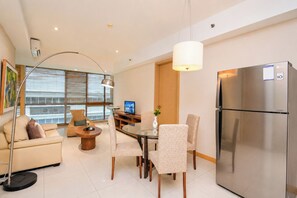 Uma sala de estar moderna com sofá, mesa de centro, mesa de jantar, cadeiras, TV, frigorífico e janelas amplas.