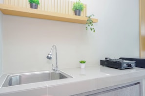 Uma cozinha moderna com uma pia de aço inoxidável, uma torneira, uma pequena planta em vaso, um fogão portátil preto e uma prateleira de madeira com duas plantas em vasos.