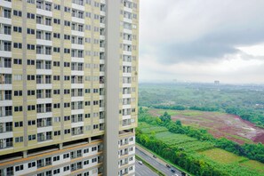 Um edifício alto com várias varandas, uma estrada com veículos e uma paisagem verde ao fundo.