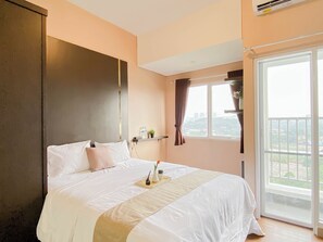 Quarto de hotel com cama, janela com vista, prateleira com objetos e ar-condicionado fixado na parede.