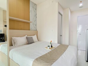 Quarto de hotel moderno com uma cama grande, cabeceira de madeira, parede de destaque em mármore, uma pequena mesa com um vaso, e uma porta à direita.