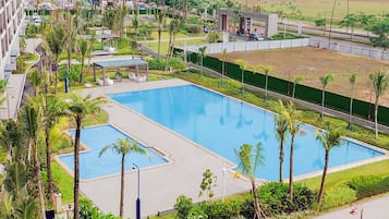 Uma grande piscina rodeada por palmeiras e vegetação, com vista para uma área residencial ao fundo.