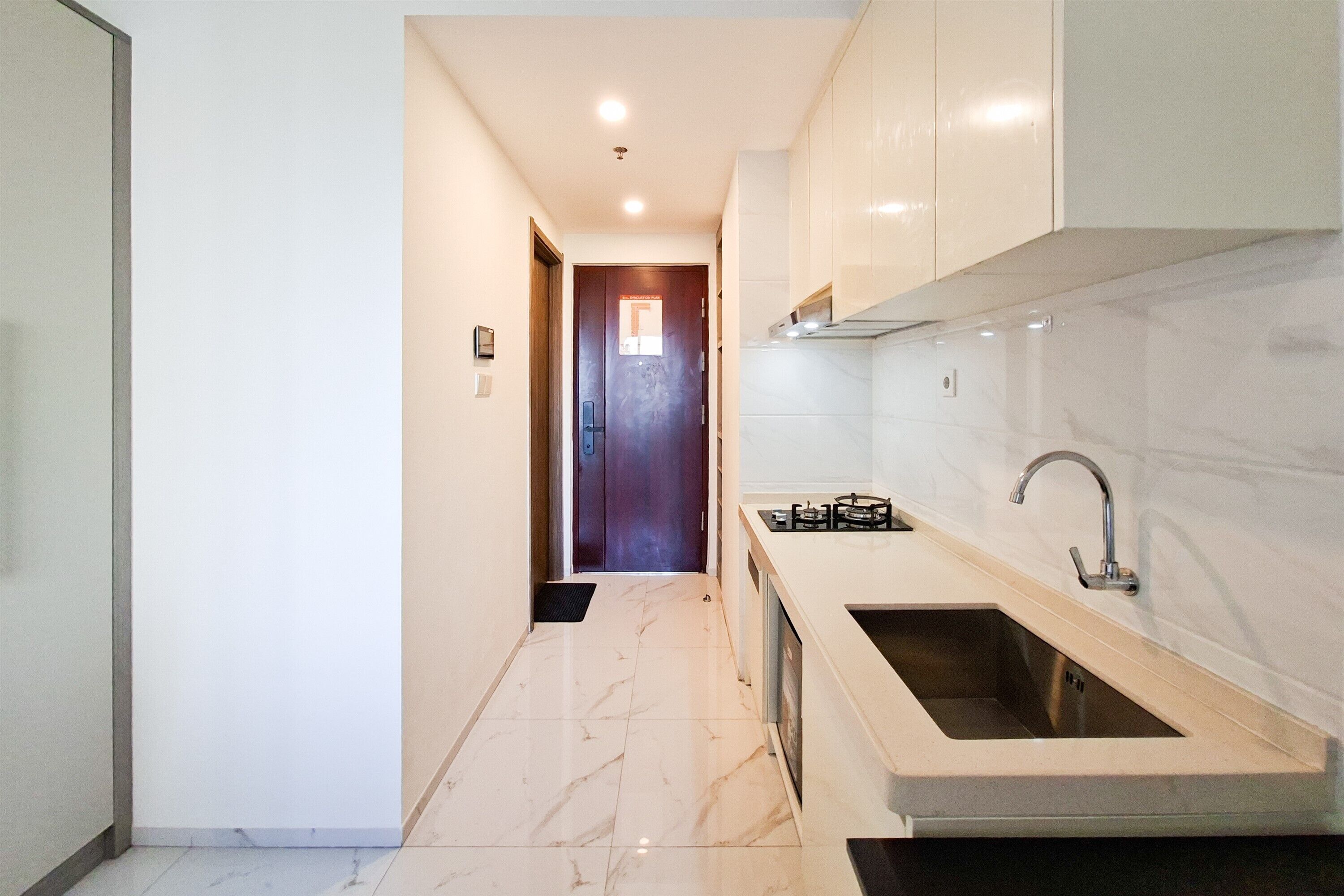 Um corredor estreito que leva a uma porta de madeira escura, uma cozinha com pia e fogão, e um chão ladrilhado.