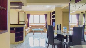 Quarto de hotel com sofá, mesa de jantar com cadeiras, televisão e um espelho grande.