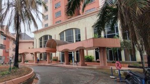 Entrada de hotel com uma entrada curvilínea, palmeiras e placa de proibido estacionar.