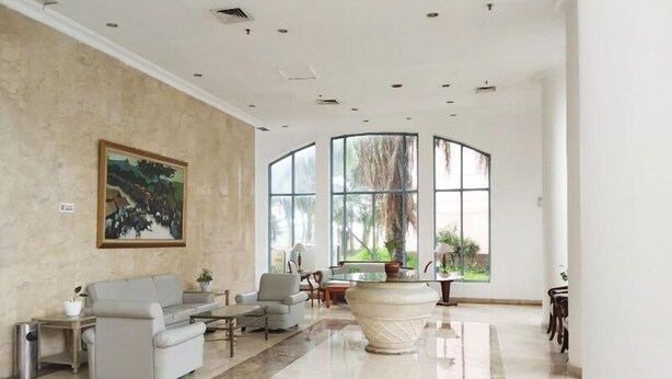 Um hall espaçoso com uma grande pintura na parede, área de estar com sofá e poltronas, e uma janela ampla que oferece vista para o exterior.