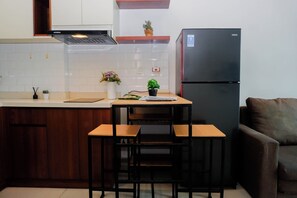Uma cozinha compacta com geladeira preta, mesa de madeira e cadeiras, bancada pequena e planta em vaso.