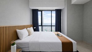 Quarto de hotel moderno com uma cama grande, cabeceira de madeira, mesa de cabeceira com um vaso e vista da cidade através de grandes janelas.