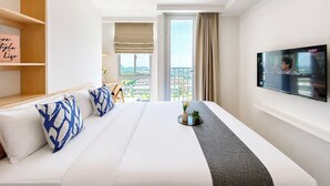 Quarto de hotel com cama, televisão, janela com vista e prateleira com um aviso.