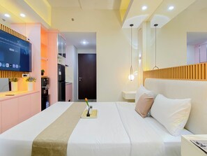 Quarto de hotel com cama, mesa de cabeceira, televisão, cozinha compacta e porta.