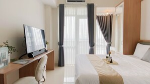 Quarto de hotel com cama, escrivaninha com computador, cadeira e ar condicionado.