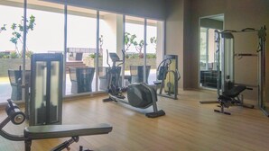 Uma academia moderna com diversos equipamentos de exercício, amplas janelas e vista para plantas ao ar livre.