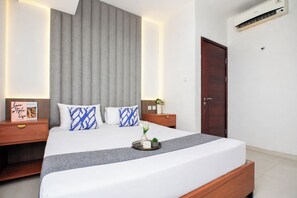 Quarto de hotel moderno com uma cama grande, mesas de cabeceira, um criado-mudo, um guarda-roupa de madeira e um ar condicionado.