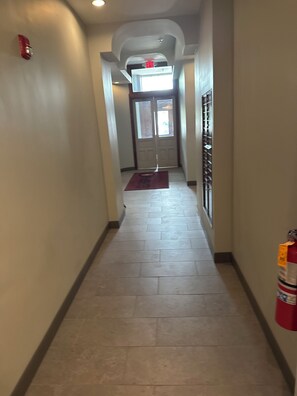 Um corredor com extintor, uma porta com janela e um tapete vermelho no chão.