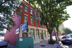 Um edifício com fachada vermelha, um letreiro com 'HILLIARD LOFTS' e uma árvore na frente.